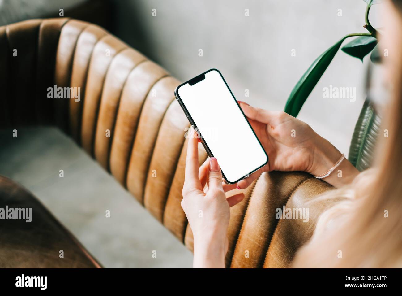 Woman holding mobile phone with white screen mock up, resting on a sofa ...