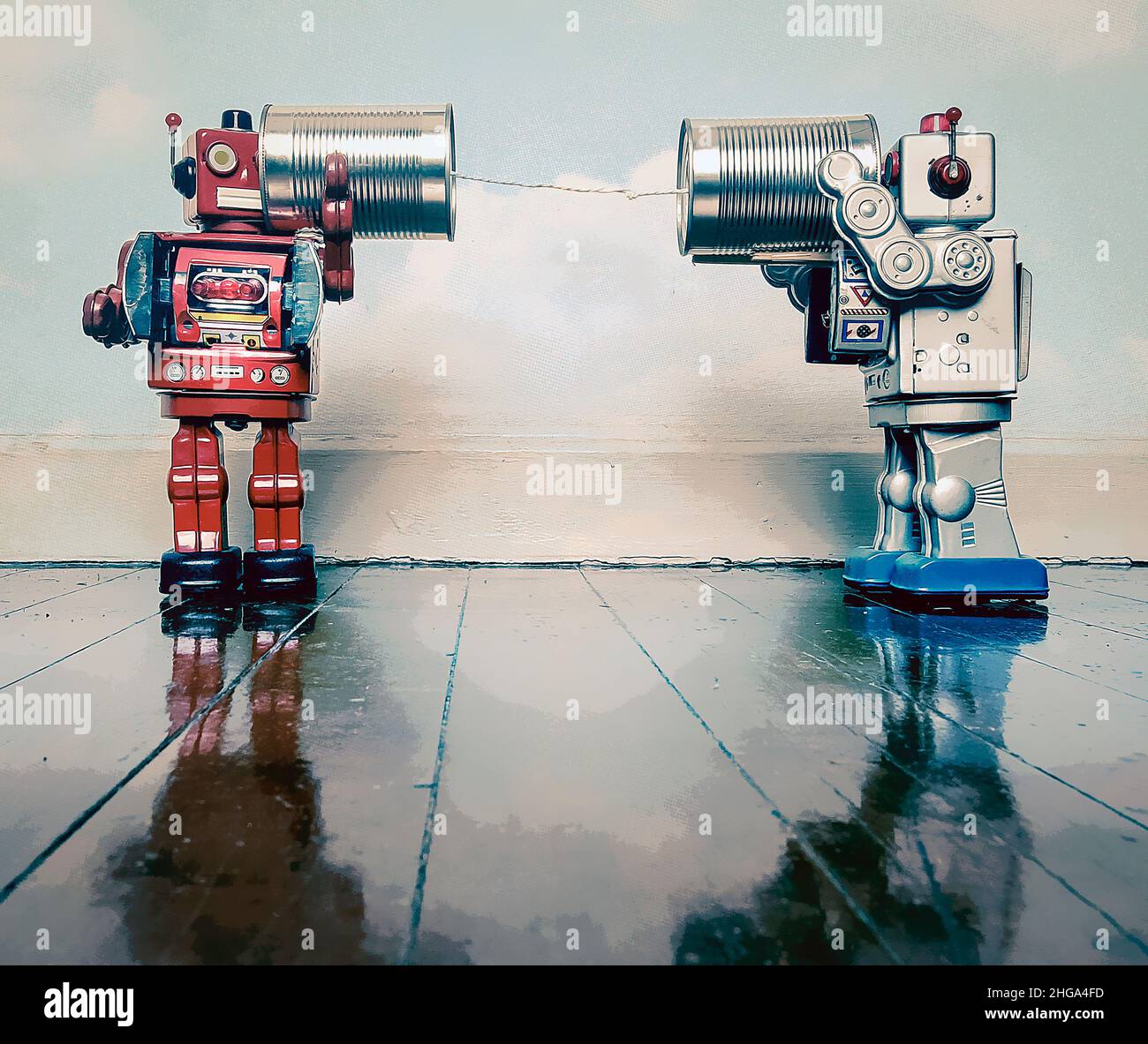 Two retro Robots toys talking on tin can phones on an old wooden floor ...