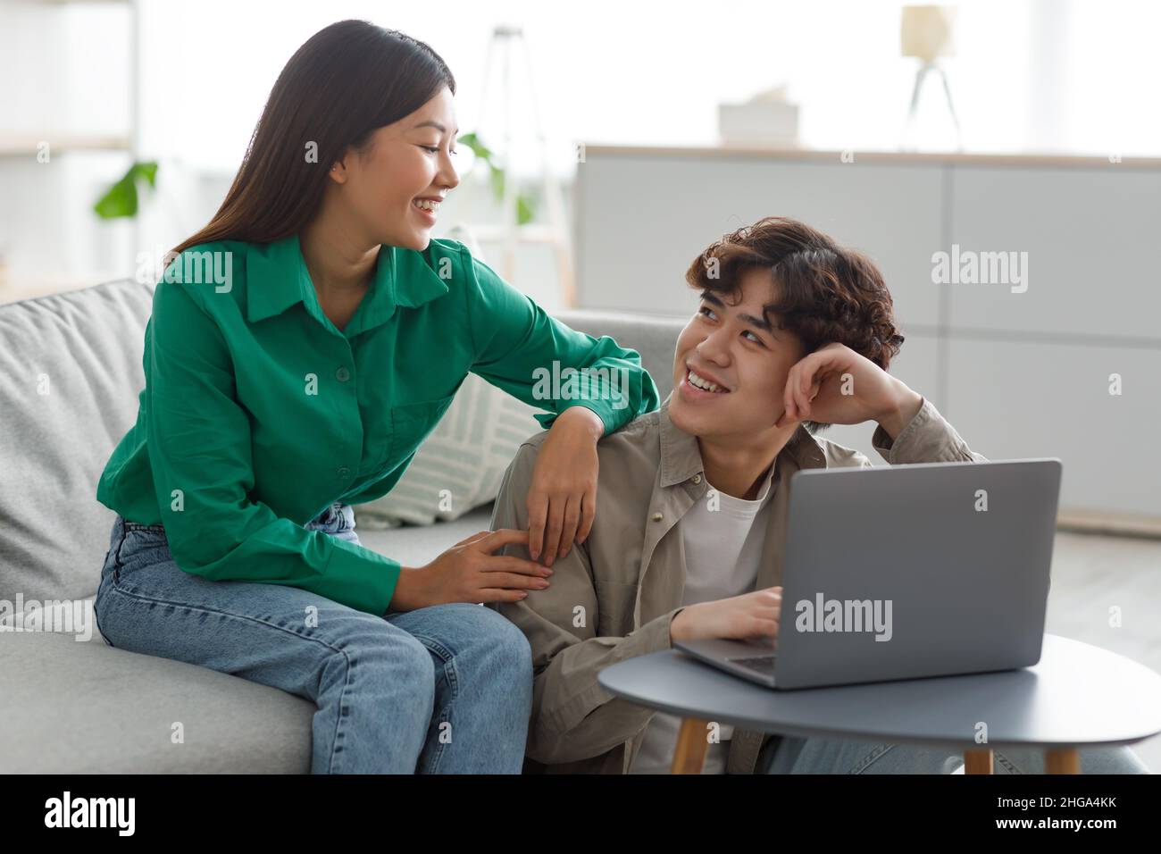 Positive millennial Asian couple using laptop computer, smiling at each ...
