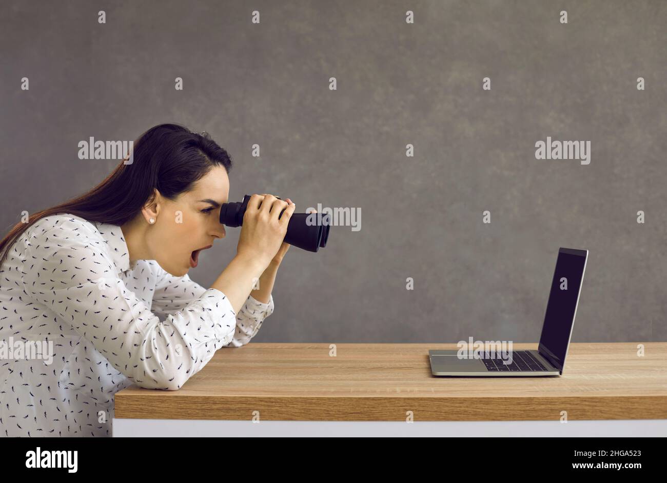 Funny shocked young woman holding binoculars and looking at screen of ...