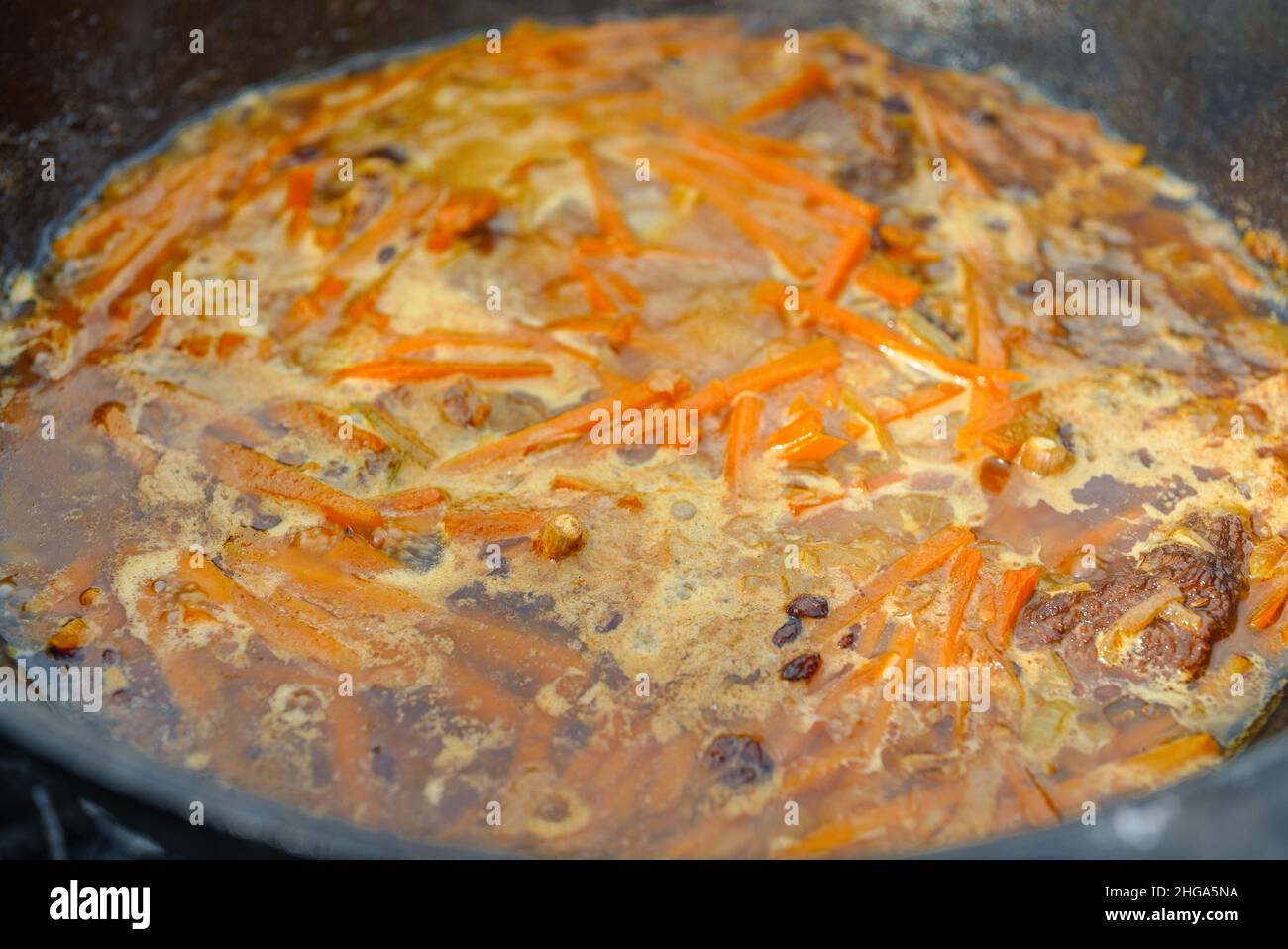 Meat with carrot is cooked in cauldron on fire. Step by step cooking of ...