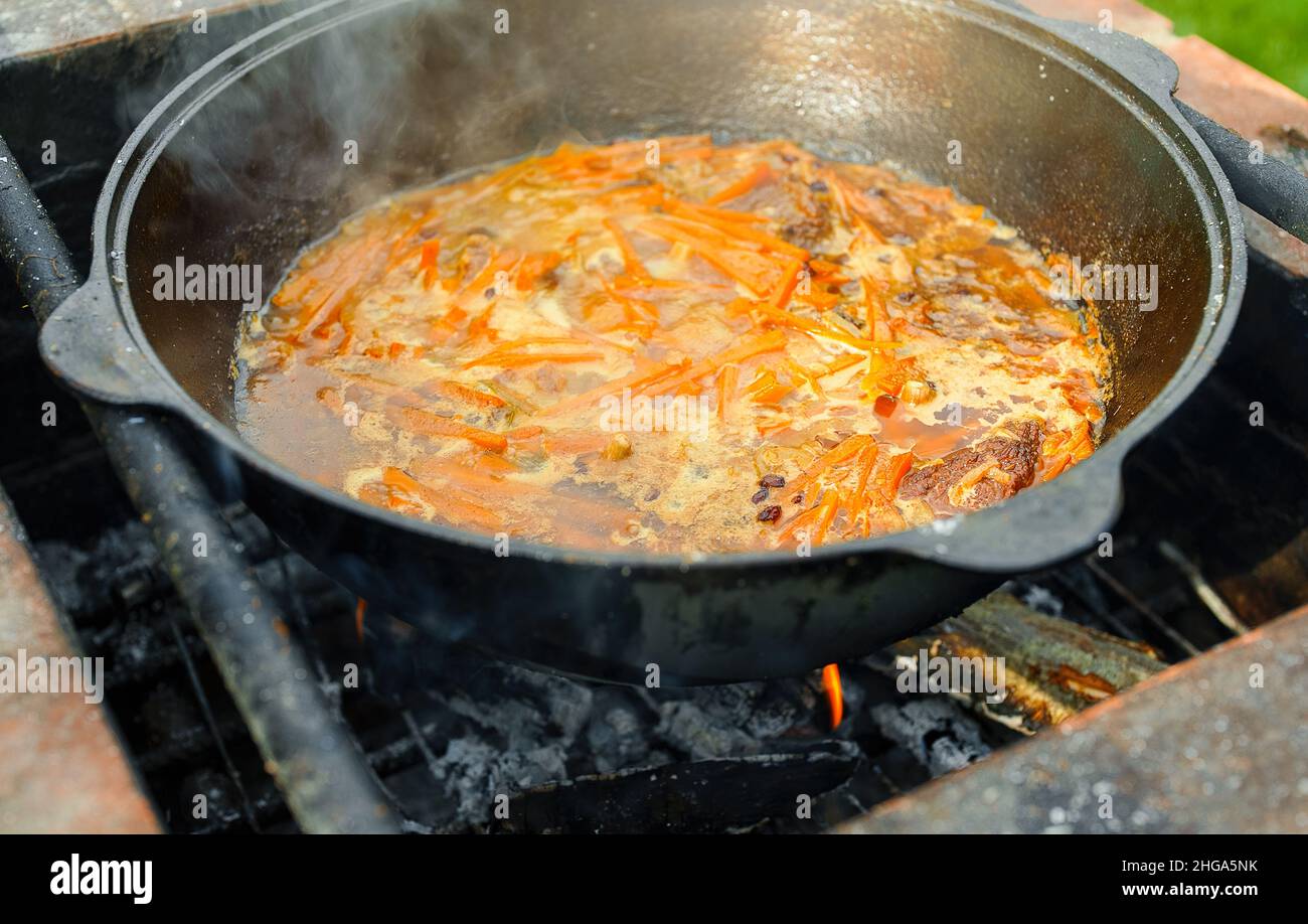 Meat with carrot is cooked in cauldron on fire. Step by step cooking of ...