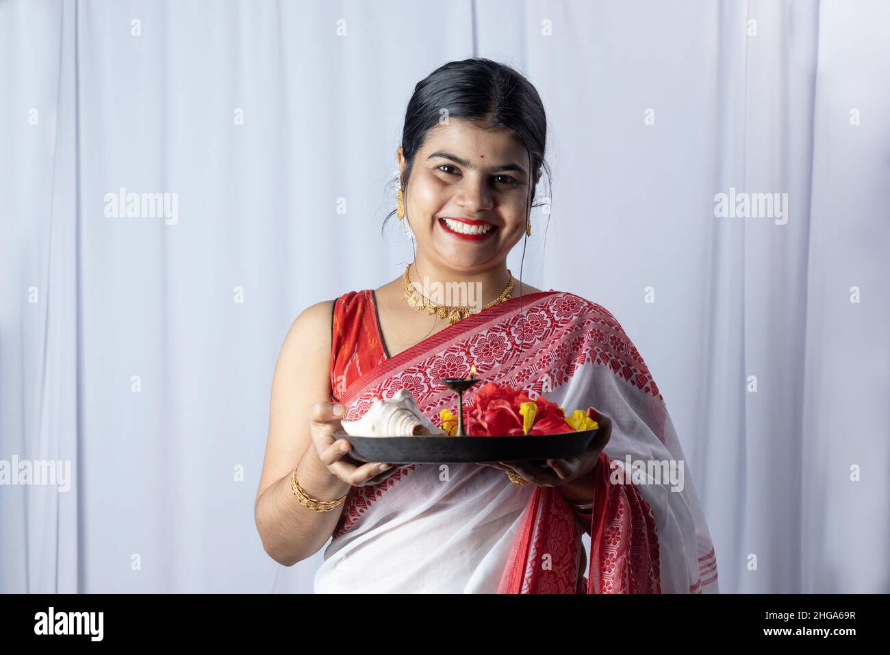 A beautiful Indian woman in red saree holding puja thali or prayer ...