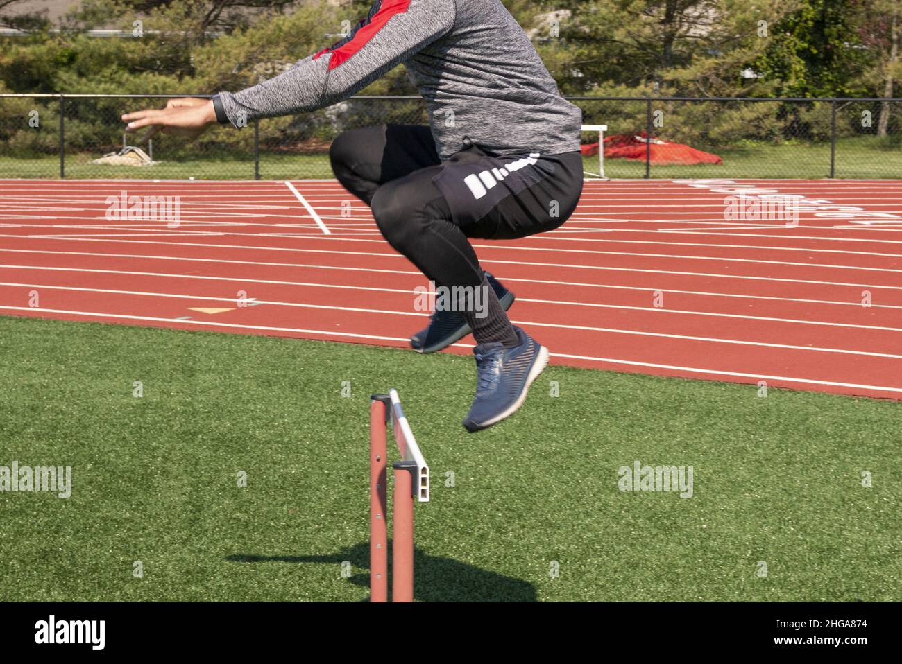 Side view of a male high school athlete jumping over a track hurdle on ...