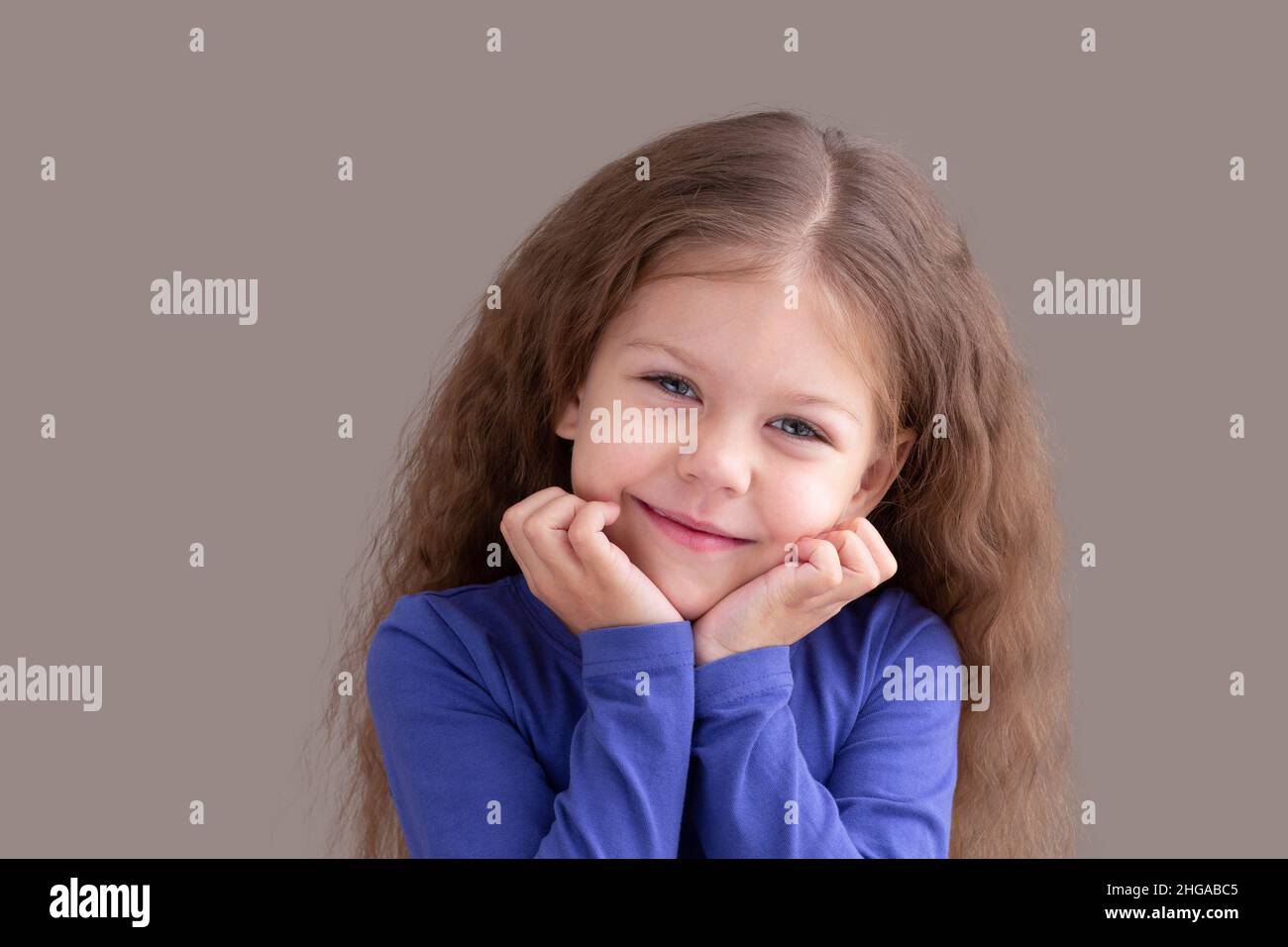 Happy and smiling child kid holding chin on fists on brown background ...