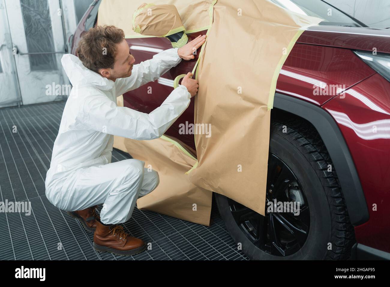 Auto painter masking car body with tape and paper before repaint ...