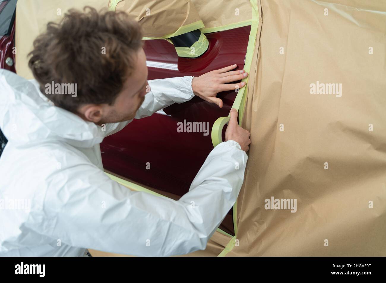 Auto painter masking car body with tape and paper before repaint ...