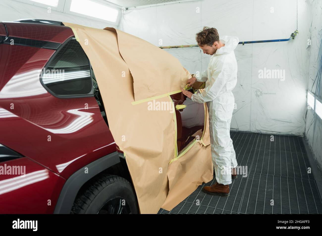Male mechanic covering body car with paper and masking tape before ...