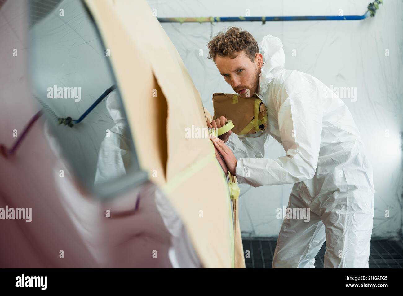 Auto painter masking car body with tape and paper before repaint ...