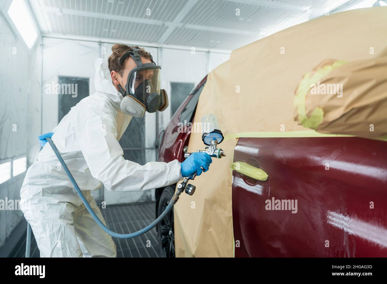 Auto painter in a protective suit and mask sprays a degreaser or other ...