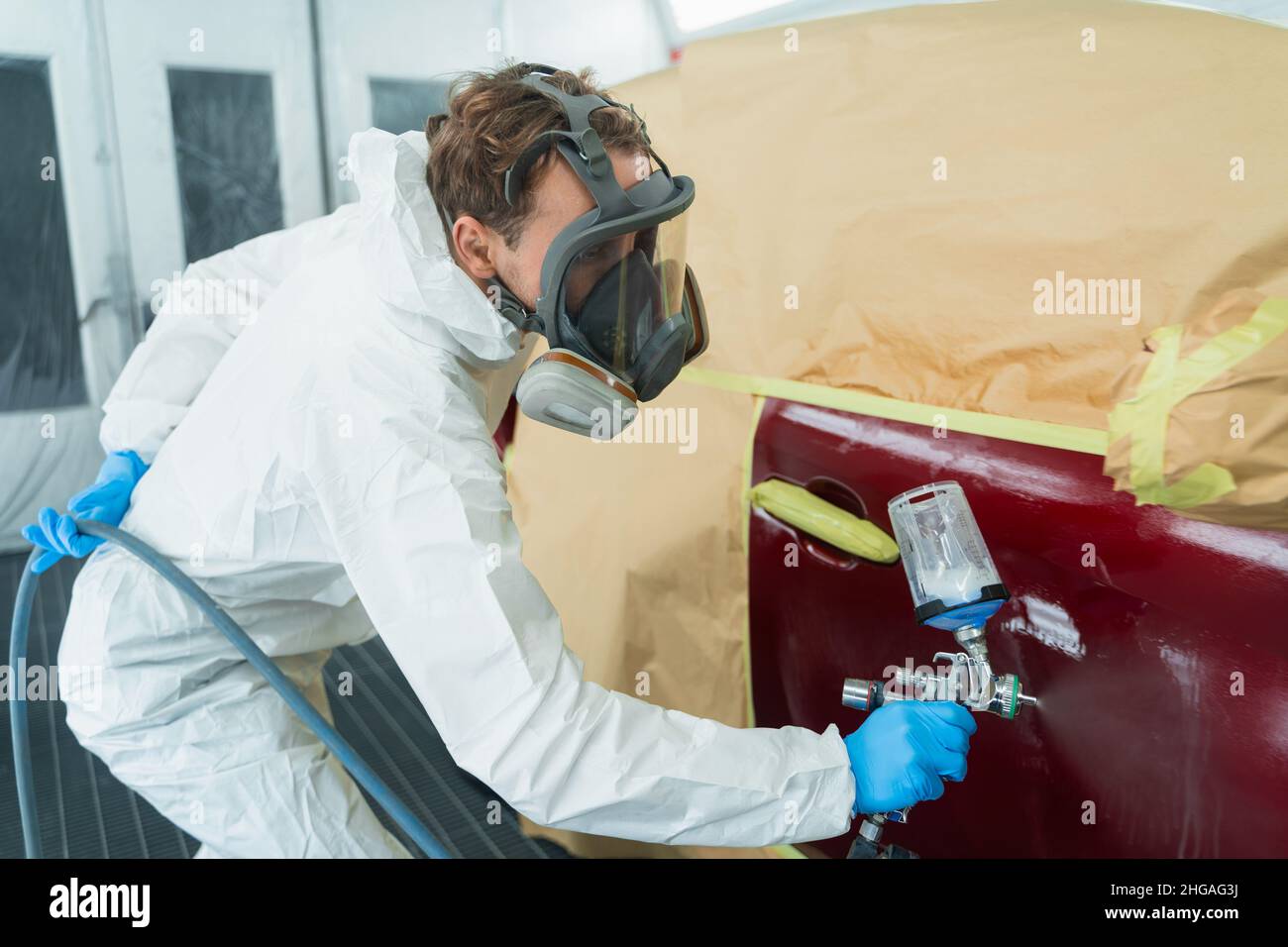 Auto painter in a protective suit and mask sprays a thinner or other ...