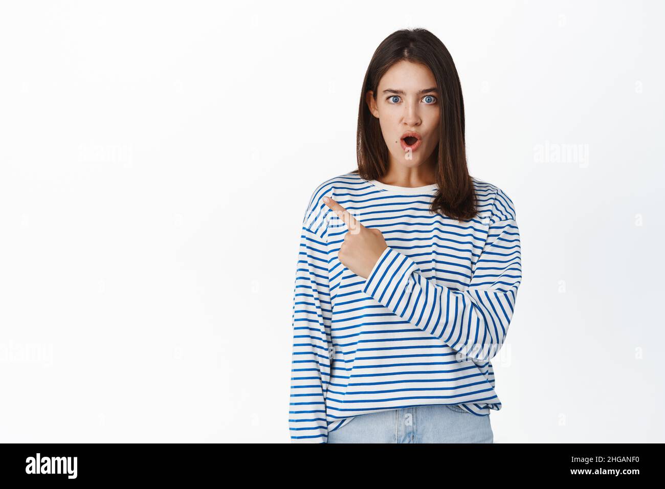 Surprised brunette girl showing advertisement, pointing at upper left ...