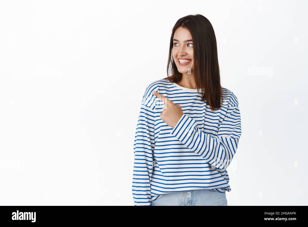 Smiling cute girl student, pointing finger and looking left at copy ...