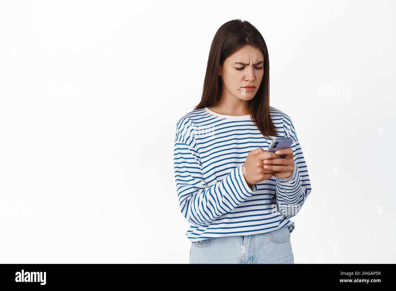 Image of complicated girl frowning while looking at phone, reading ...