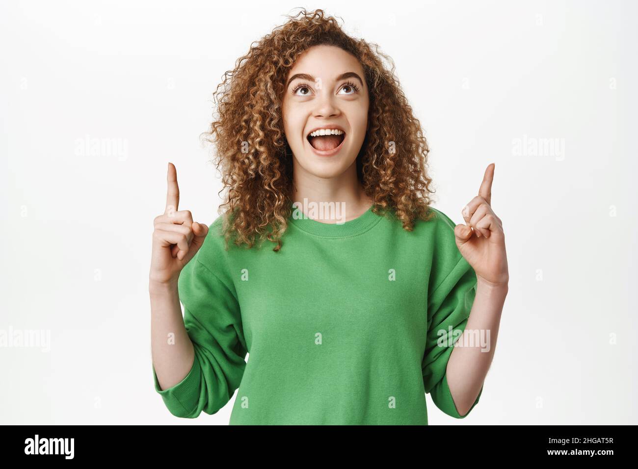 Happy smiling curly-haired woman looking with amazement up, pointing ...