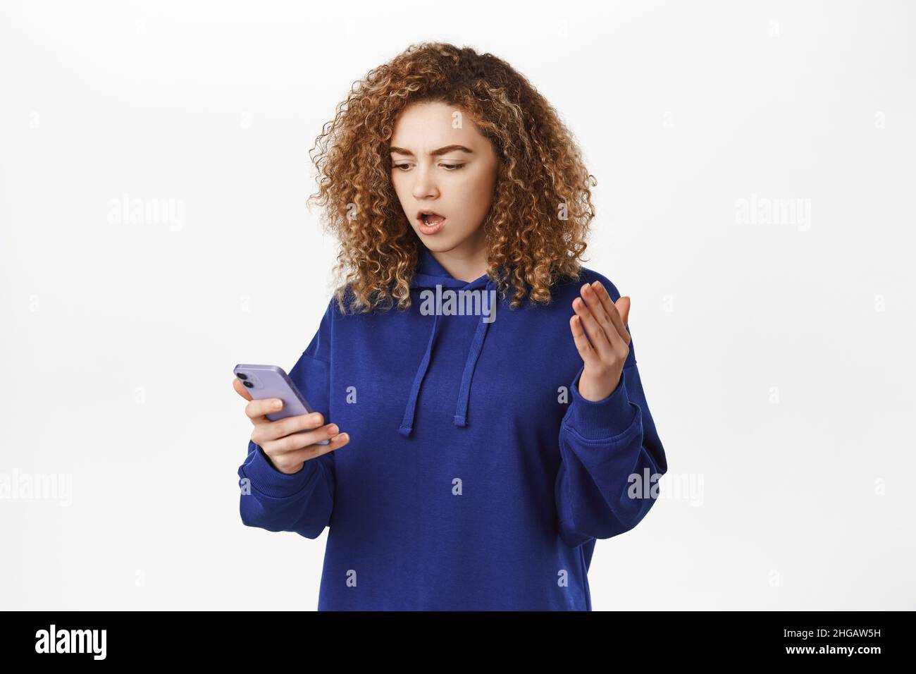 Image of confused young woman complains at mobile phone, argues with ...