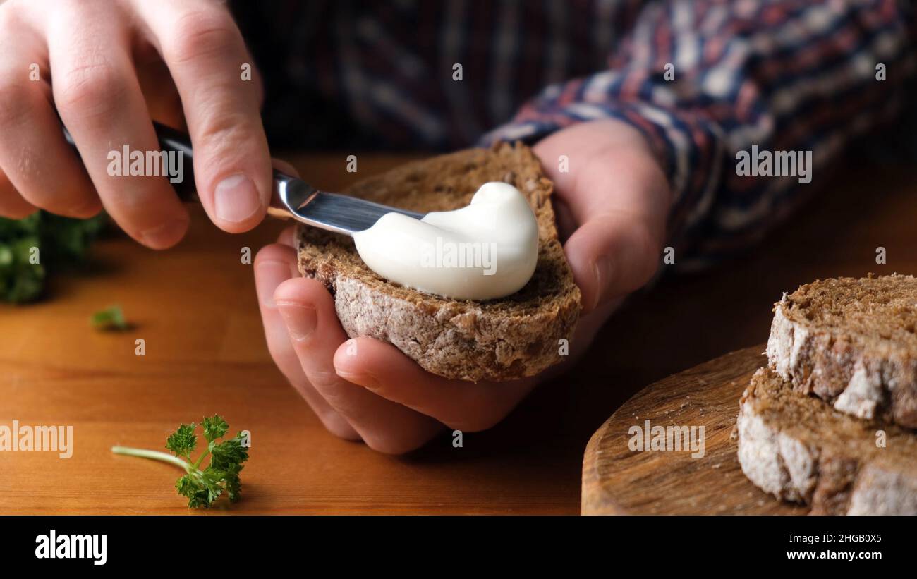 Spreading cream cheese on rye bread. Male person making toast with soft ...