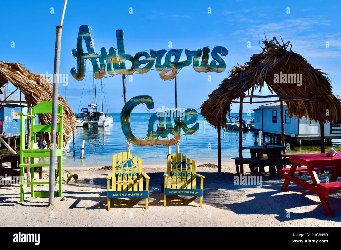 An Ambergris Caye sign with two beach chairs below it and table benches ...
