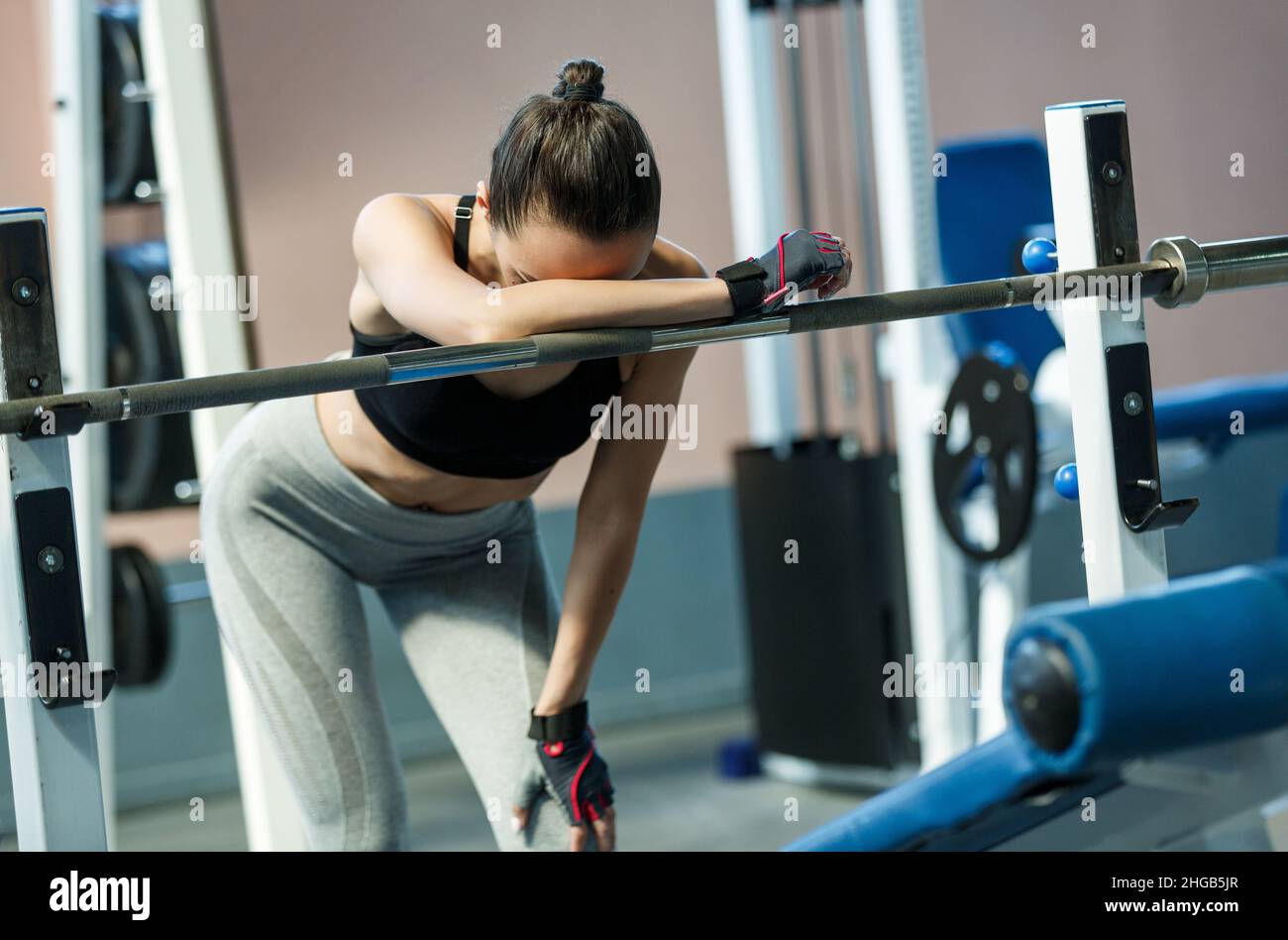 Exhausted girl in a gym taking a break leaning on a barbell. Workout ...