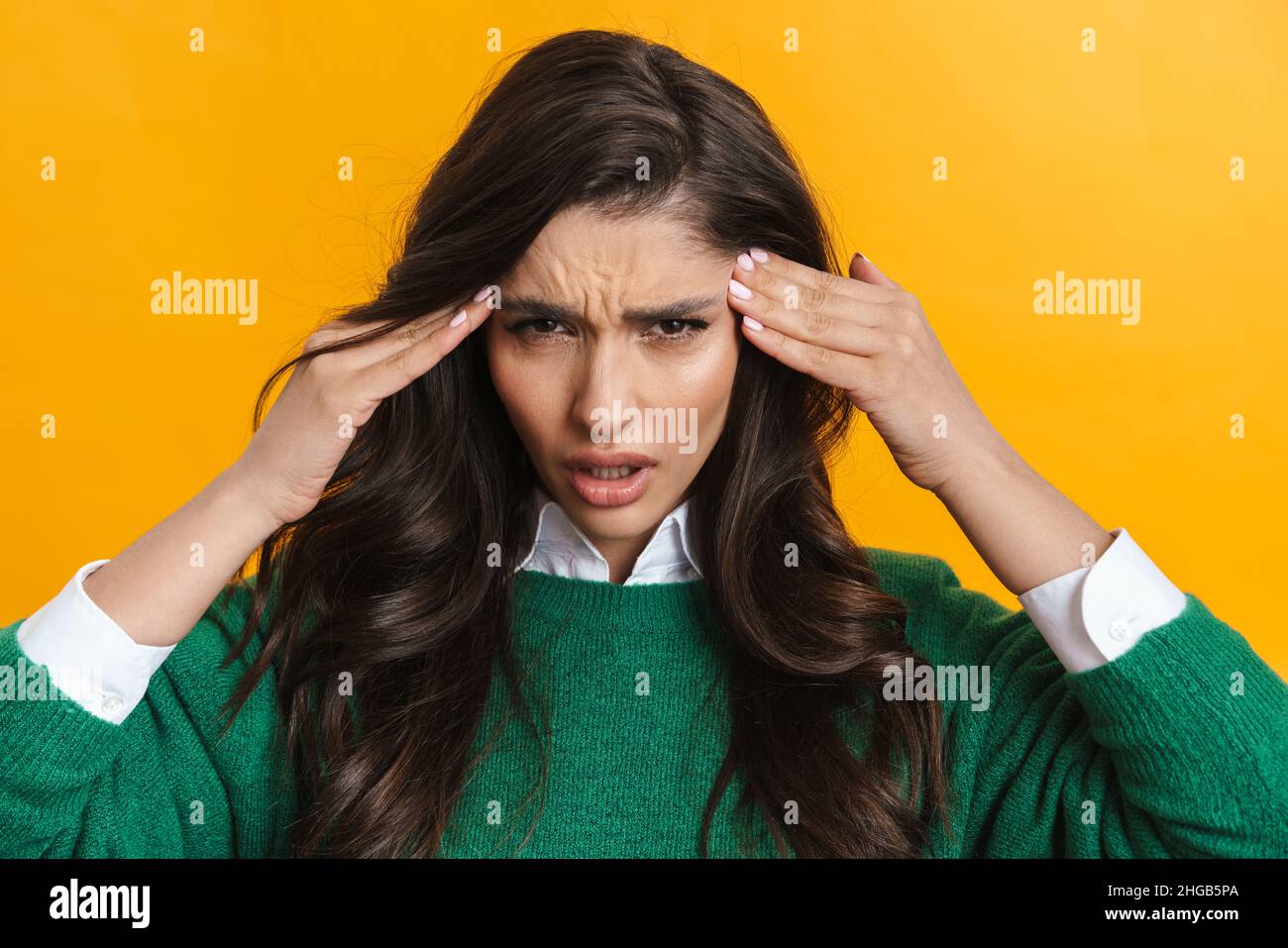 Portrait of a frowning casual woman standing over yellow background ...