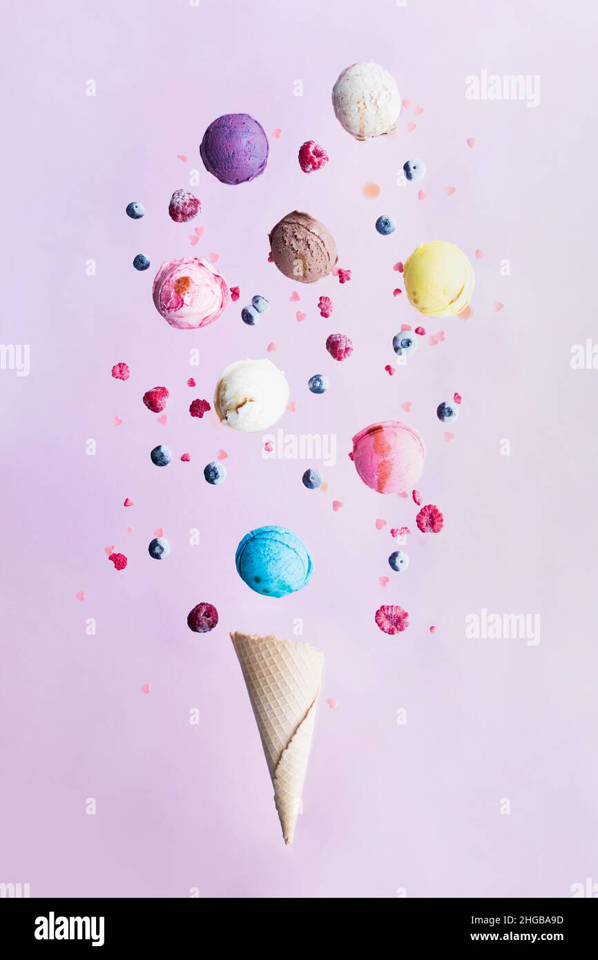 Falling ice cream scoops and berries into the vafel cone on pink ...