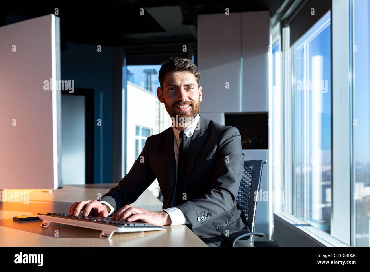 Happy and smiling businessman working in modern office by the window at ...
