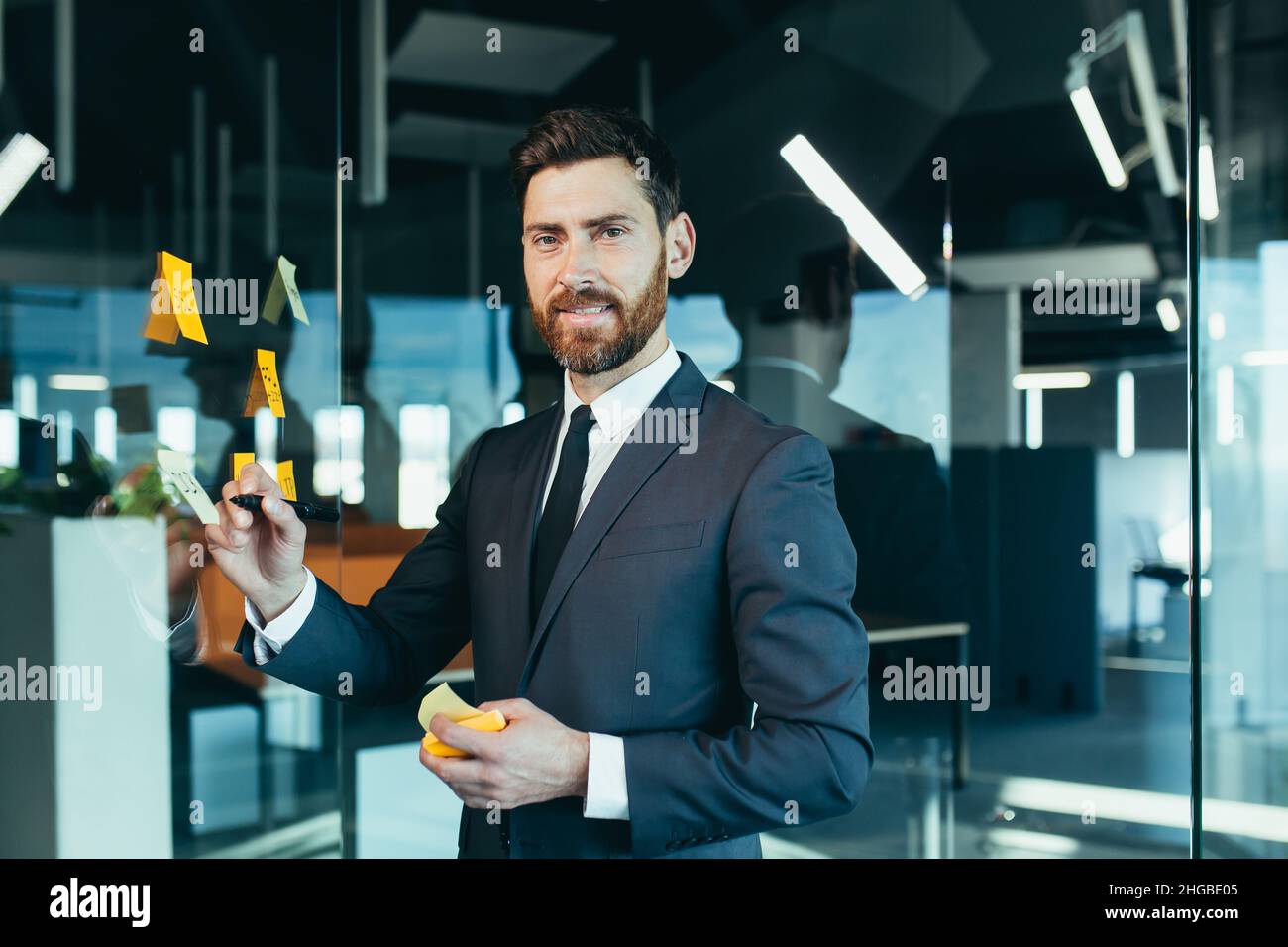 Successful manager looks at camera and smiles, businessman writes on ...