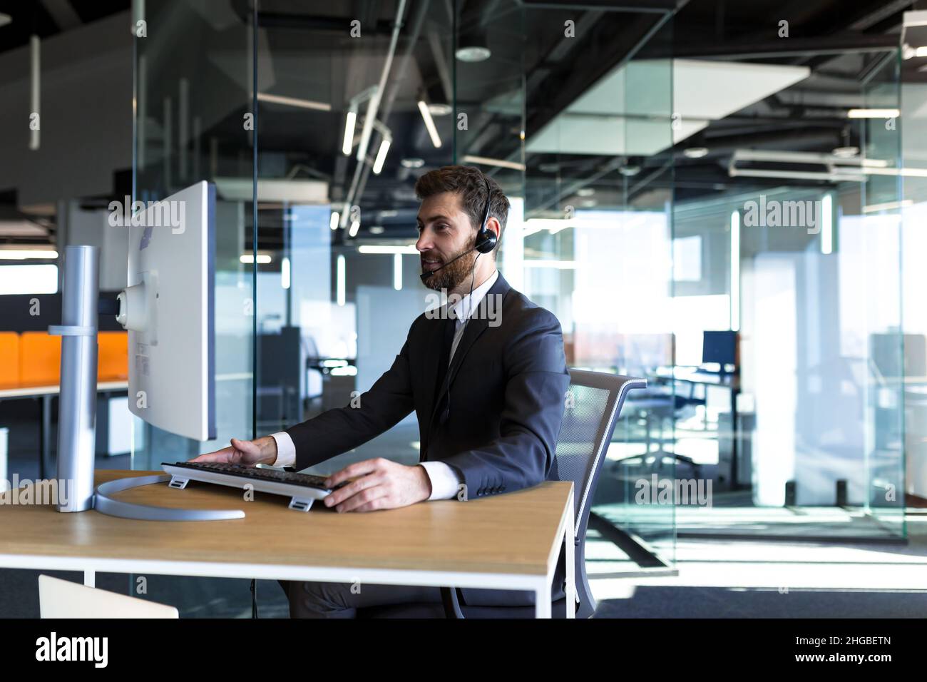 Business man in a modern office works at a computer, uses a headset for ...