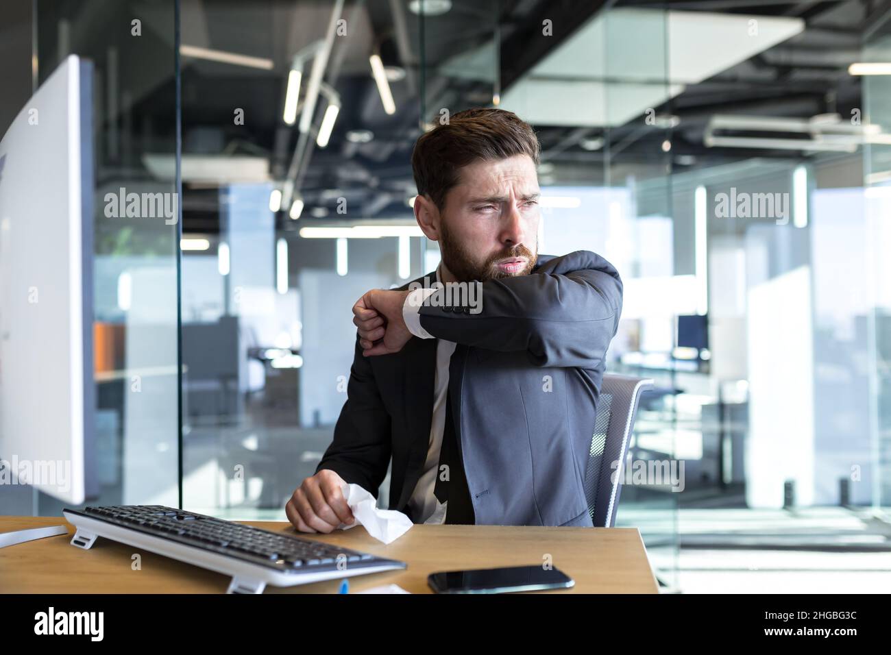A man sneezes working in the office, a worker sick at work with a ...