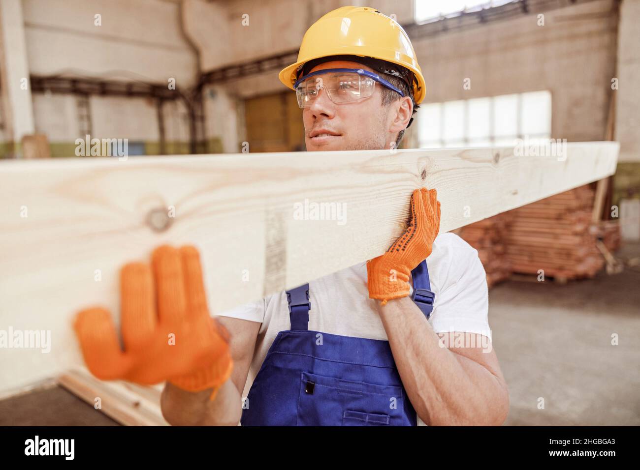 Good-looking male builder carrying wooden plank at construction site ...