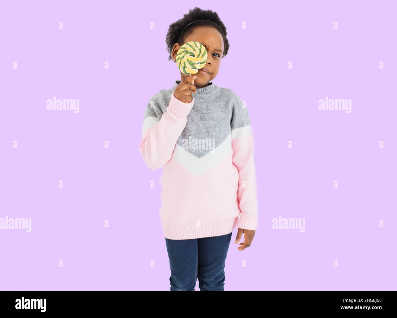 African little child using sweet lollipop for hiding one eye in studio ...
