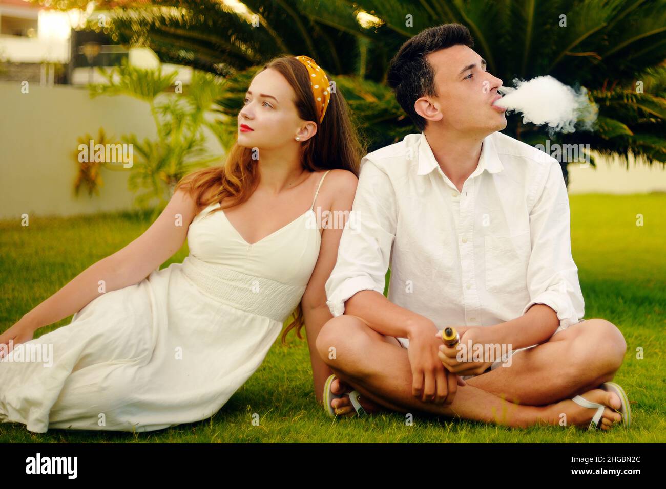 A vape woman and man. Couple on vacation, under a palm tree. Rest ...