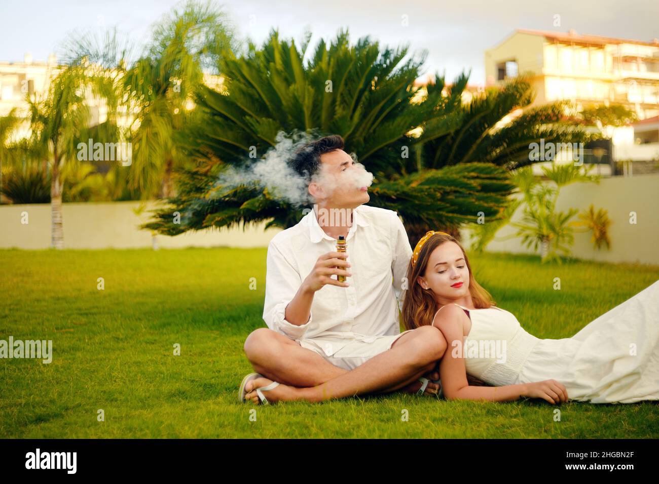 A vape woman and man. Couple on vacation, under a palm tree. Rest ...