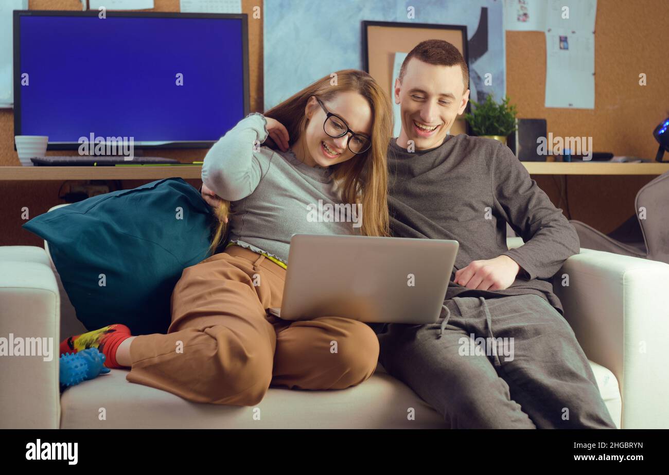 A couple is sitting on a couch and looking at a computer. The couple ...
