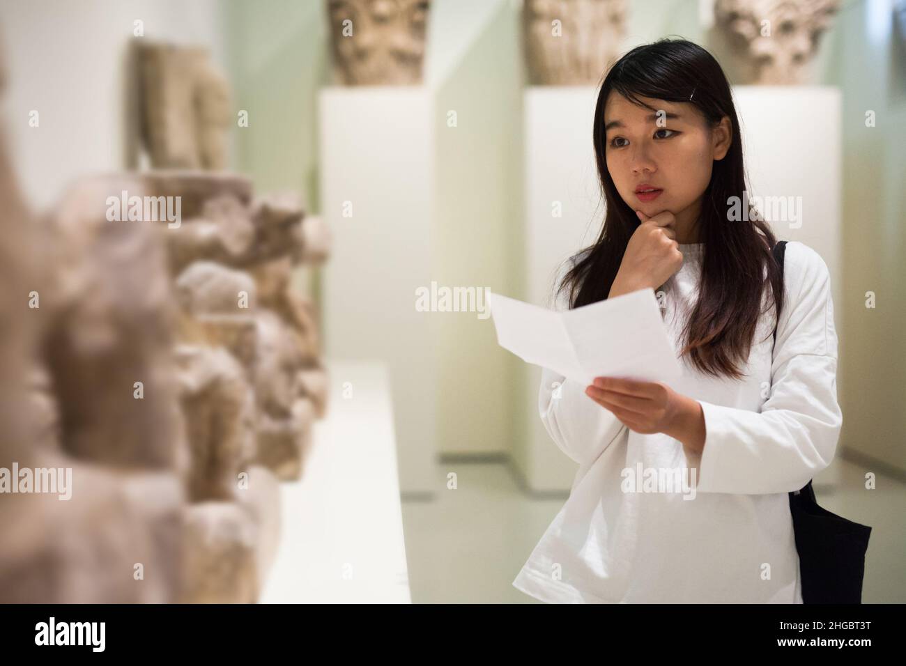 Chinese woman visitor with guide book looking at exhibition in museum ...