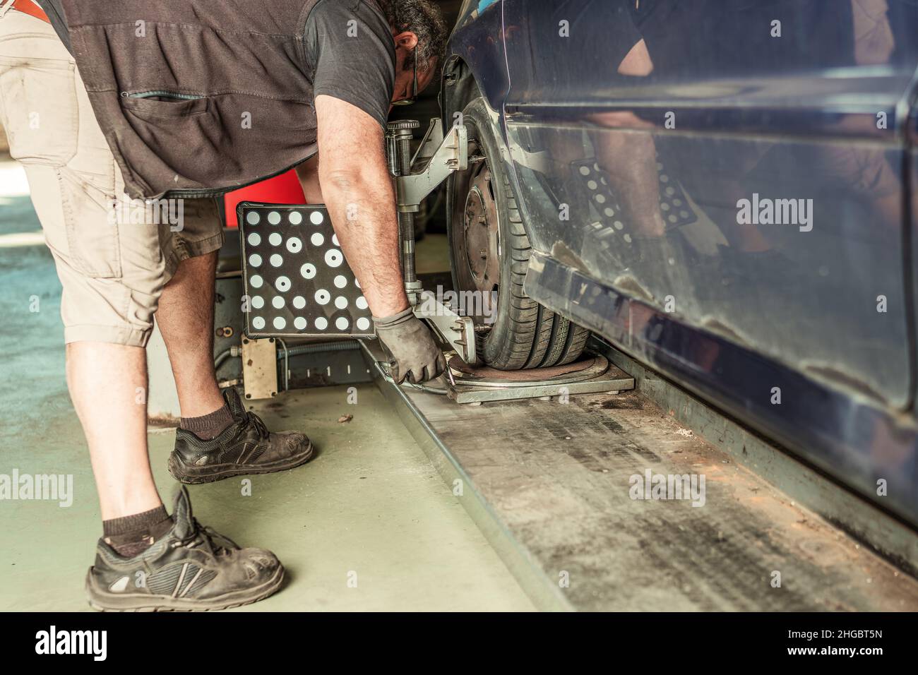 Mechanic crouched to align the steering of a car lifted by a jack in a ...