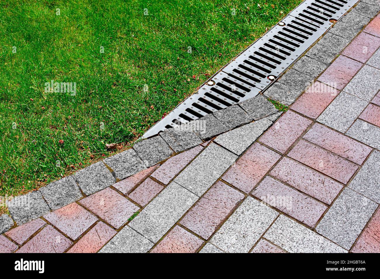 drainage grate bolted to storm drain at corner of pedestrian pavement ...