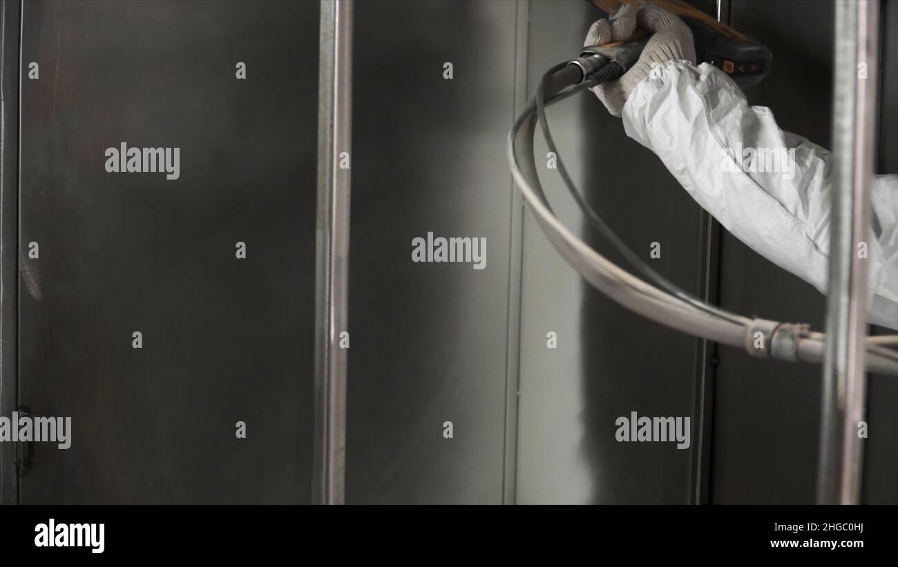 Worker at factory painting metal details with a gun of powder coating ...