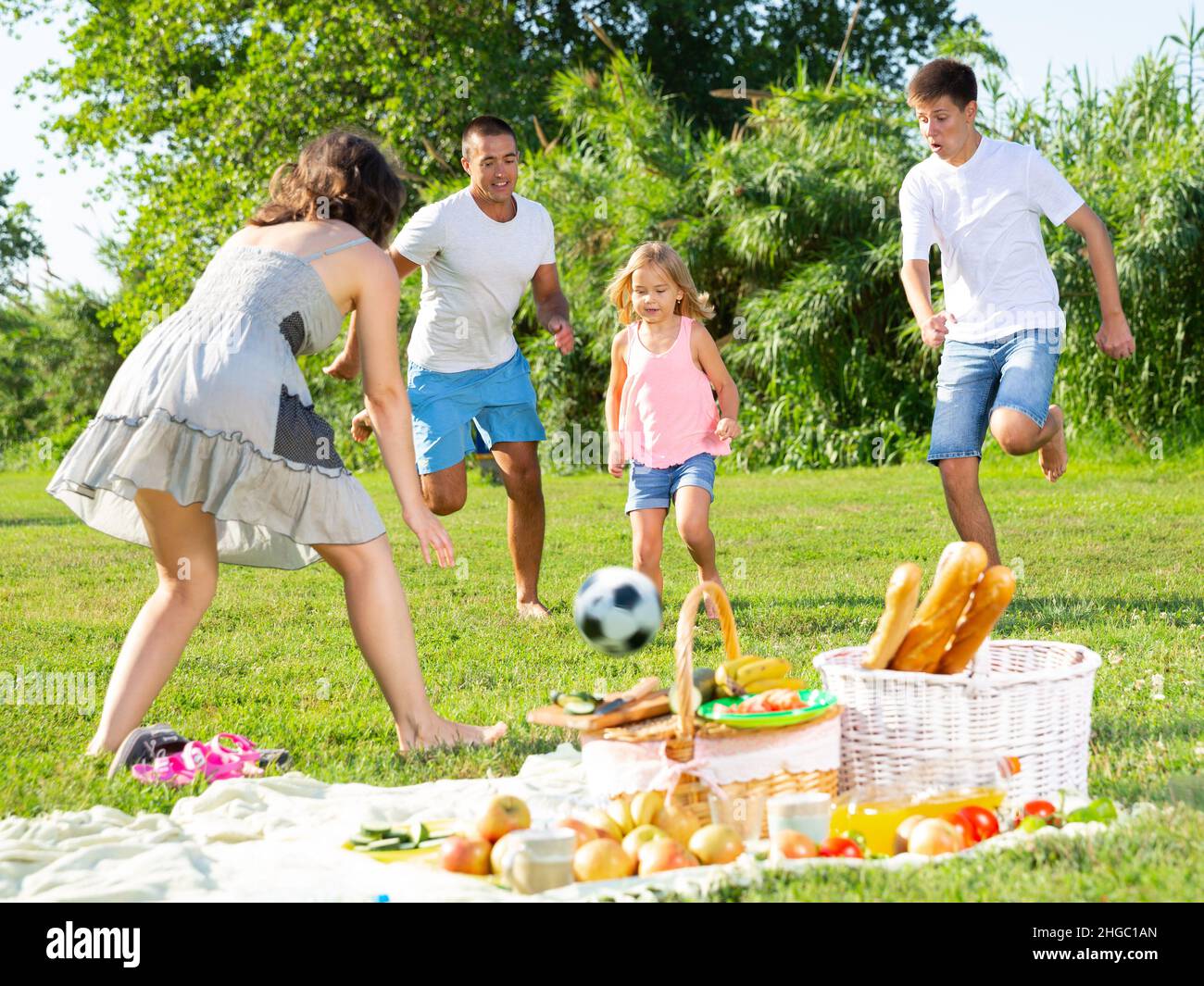 Positive parents with two kids playing soccer together on green field ...