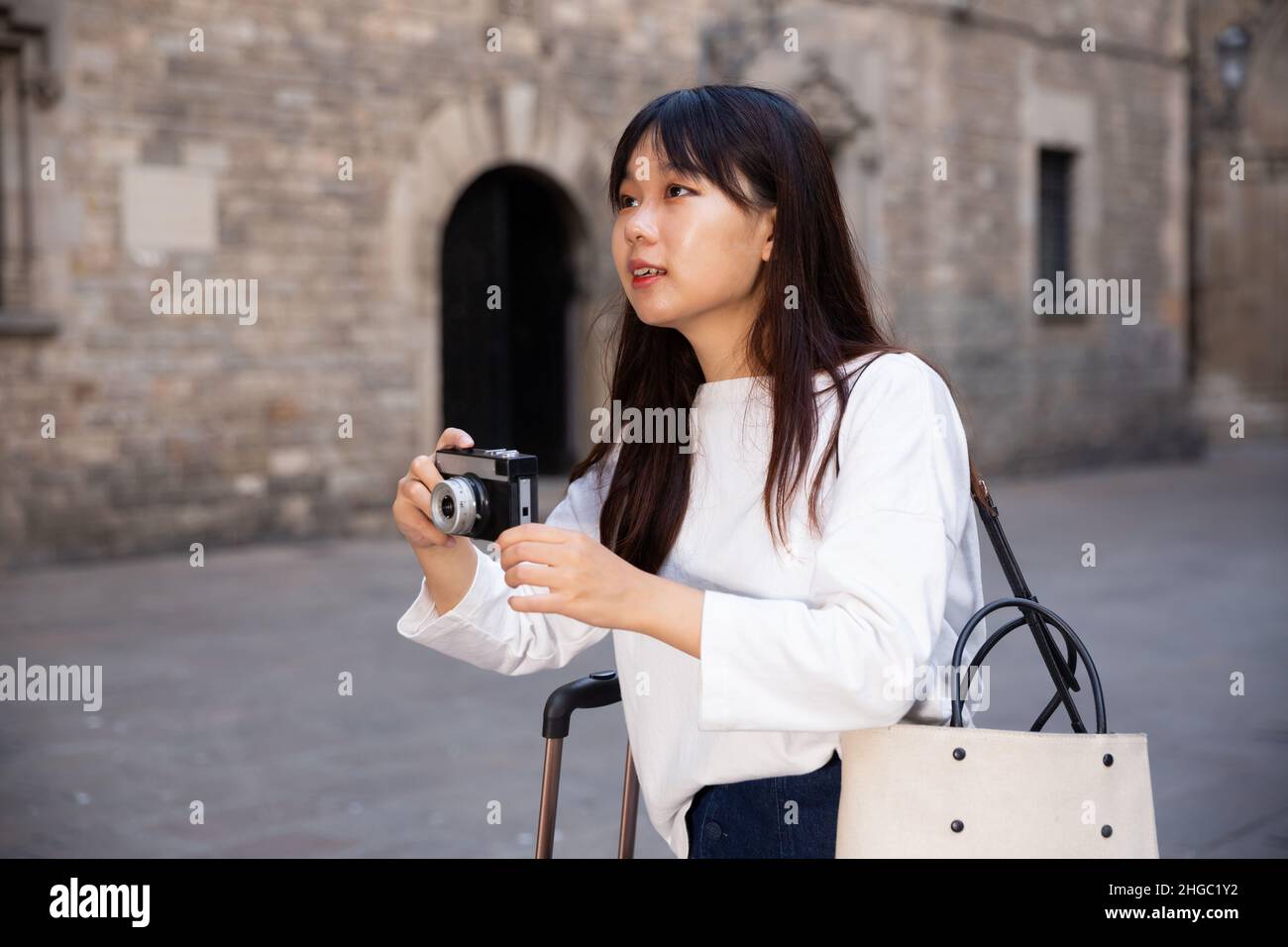 Young chinese woman traveler strolling with luggage around city, making ...