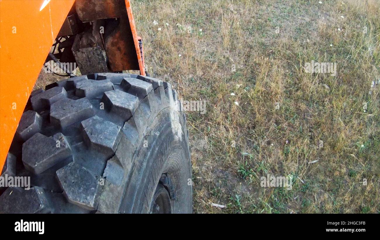 View from a wheel of heavy truck moving on withered grass meadow. Close ...