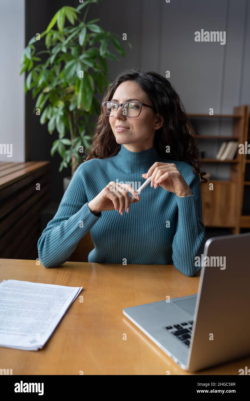 Smiling happy female employee at workplace looking in window and ...