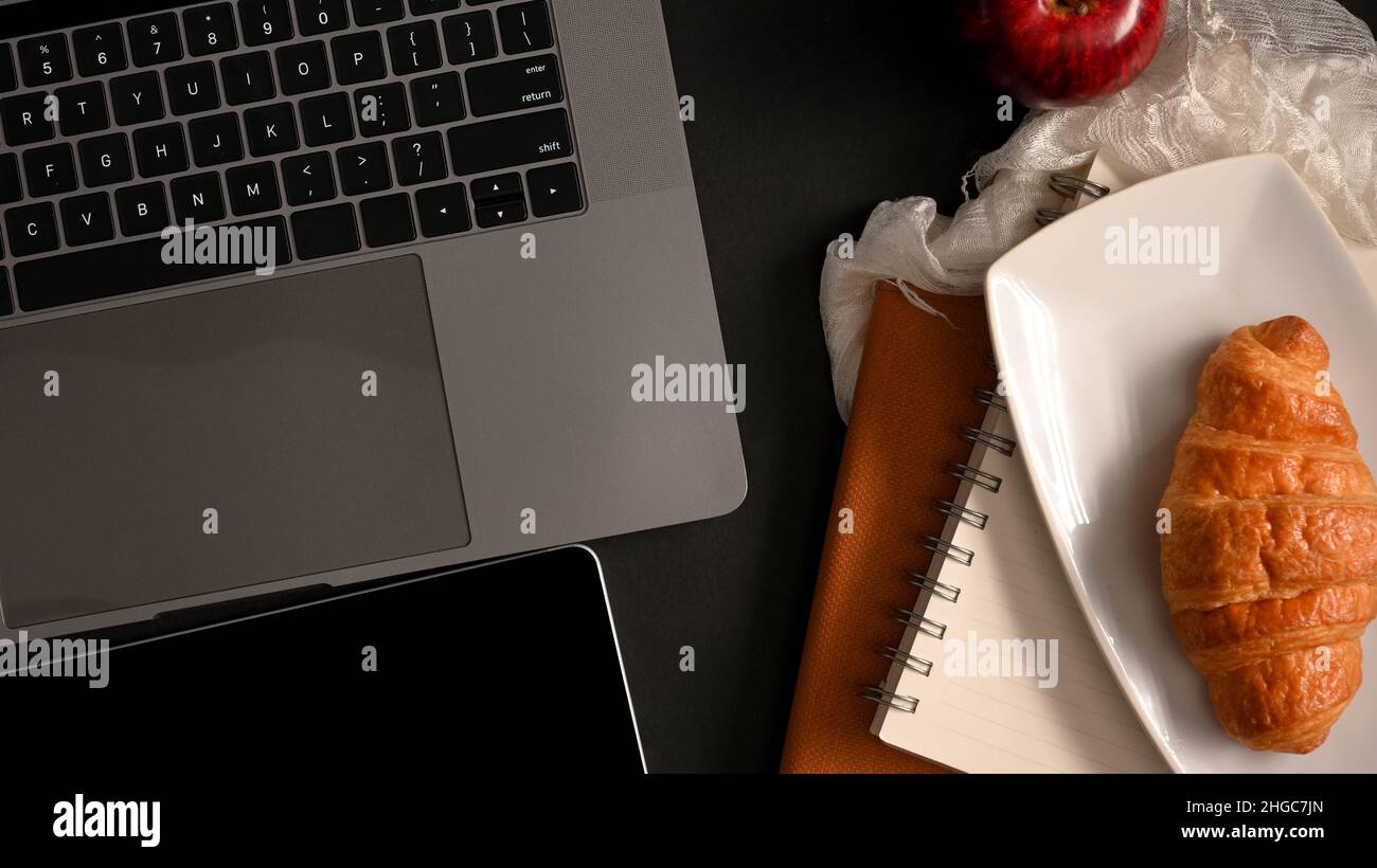 Modern dark workspace with laptop computer, notebooks and croissant on ...
