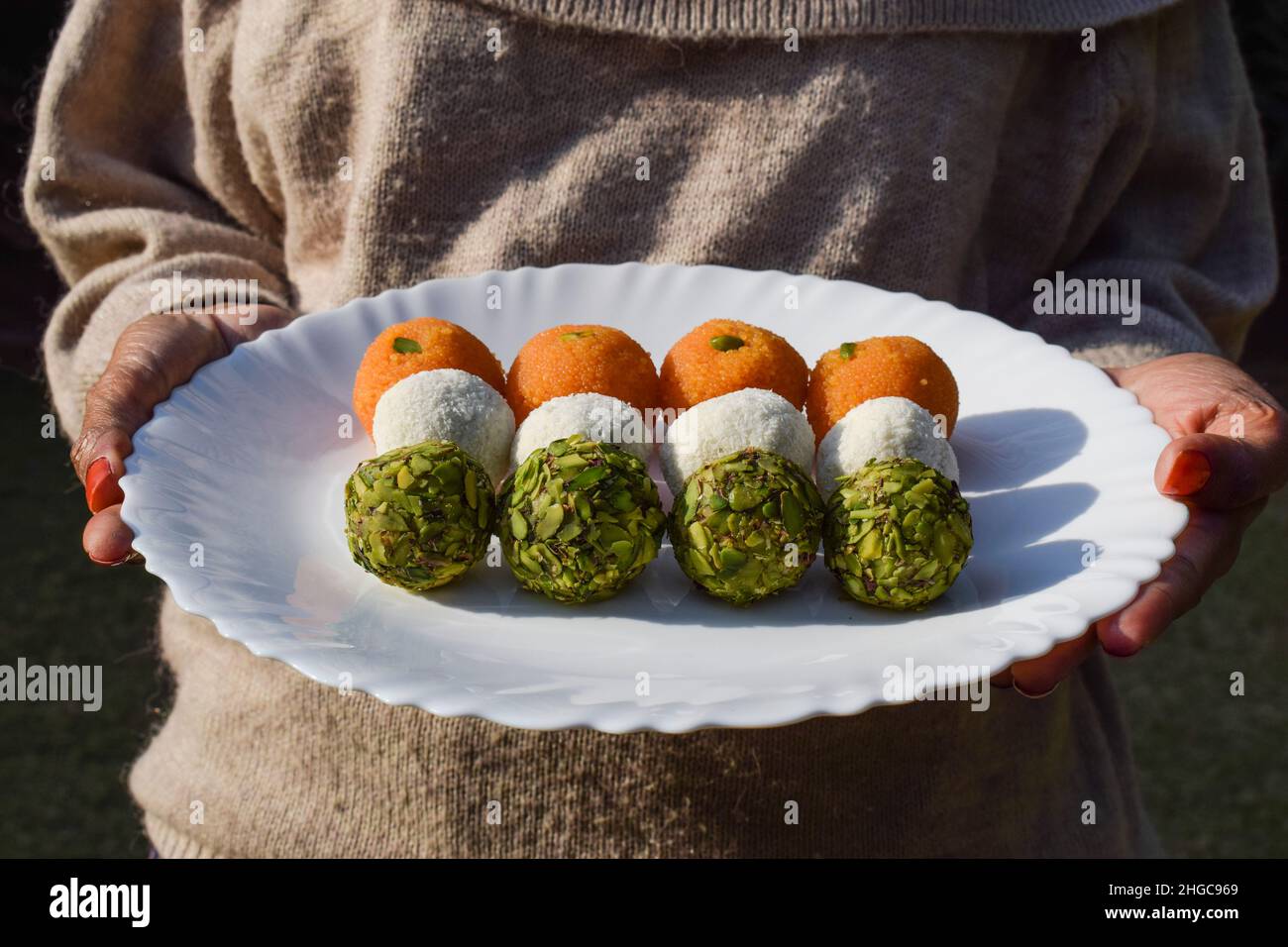 Female holding plate of Tricolor food with three types of ladoo colors ...