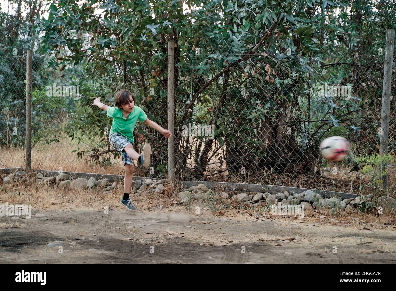 portrait of a little boy hitting a soccer ball in a field between trees ...