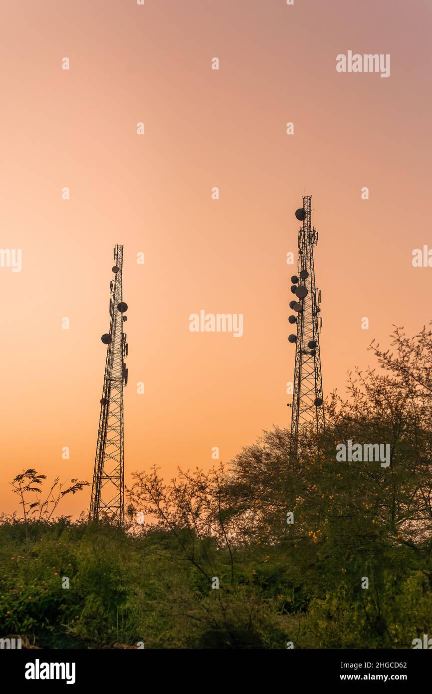 Sunset view of two telecom towers with tree and bushes in the ...