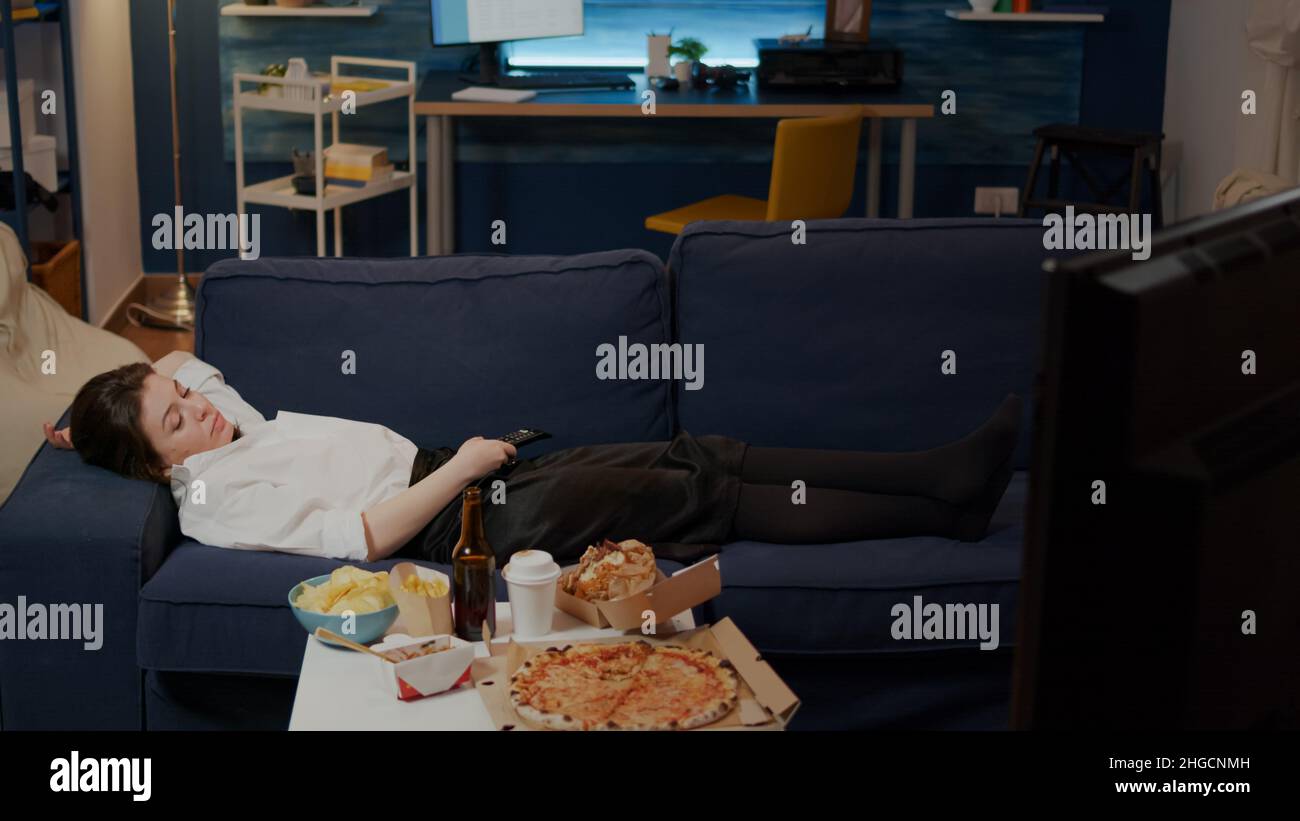 Sleepy adult relaxing on sofa after eating takeaway meal while watching ...