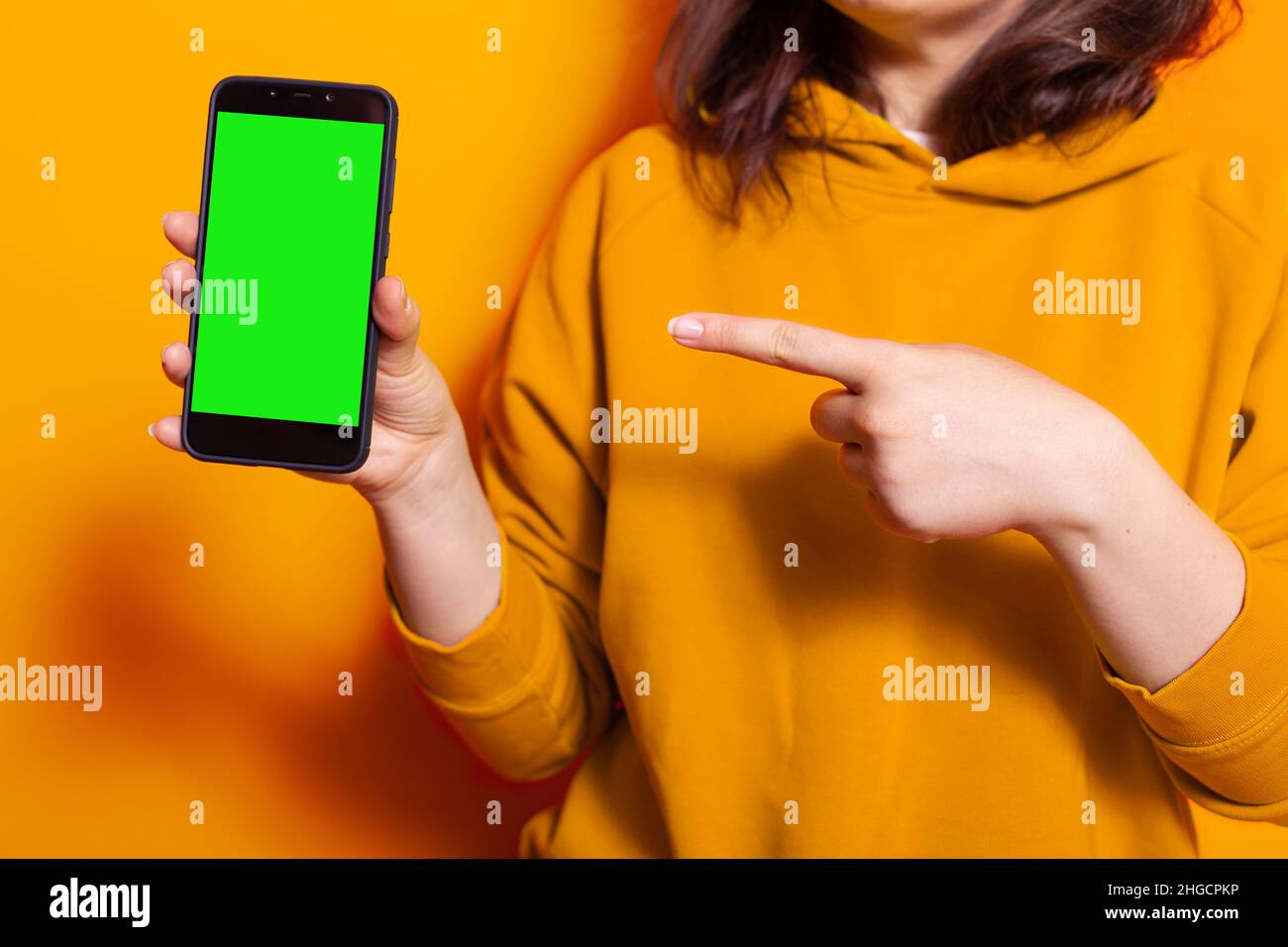 Close up of woman pointing at vertical green screen on phone. Person holding isolated mockup ...