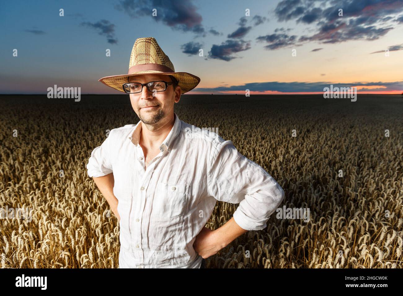 Farmer in a straw hat and glasses standing in a ripe wheat field before ...