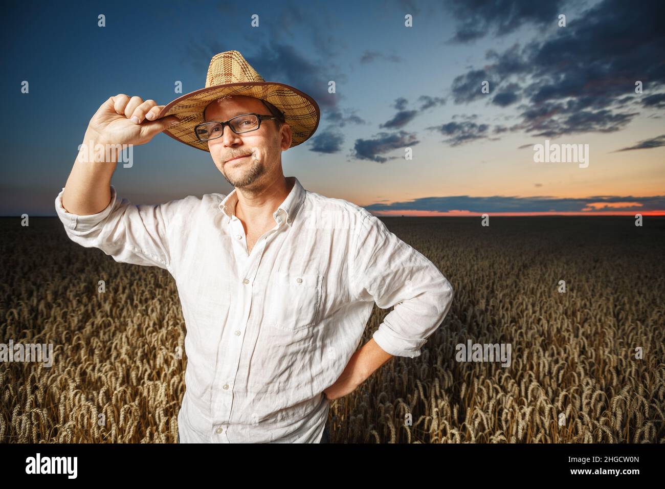 Farmer in a straw hat and glasses standing in a ripe wheat field before ...